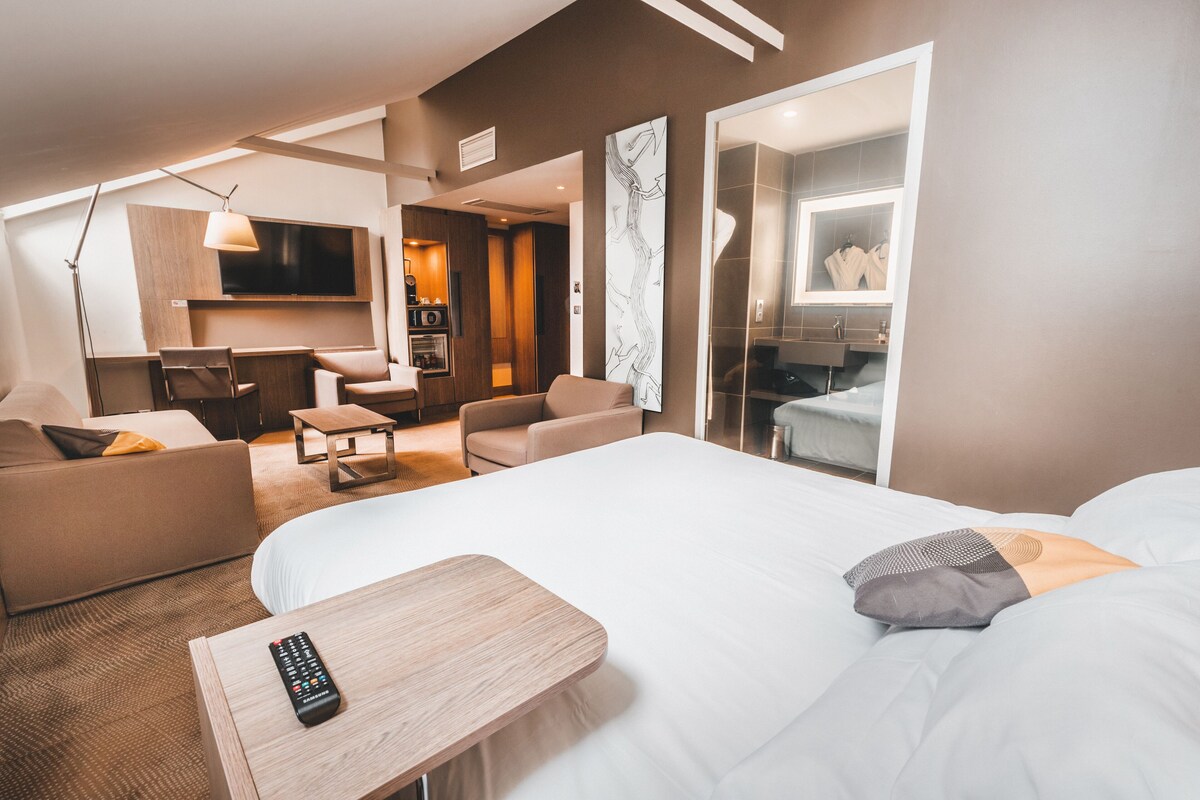 Quarto de hotel com uma cama grande, uma escrivaninha, um sofá e uma televisão.