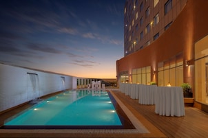 Piscina com vista para o pôr do sol, um deck de madeira e um edifício com grandes janelas.