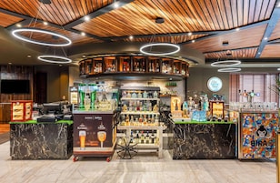 Uma área de bar com balcão circular, prateleiras com garrafas de bebidas e uma placa com a inscrição 'The Low Bar'.