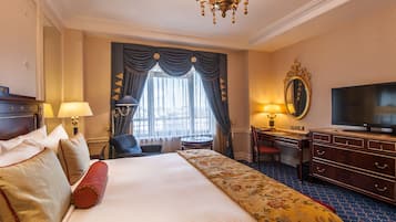 Quarto de hotel com uma cama grande, uma escrivaninha, uma televisão e vista para a cidade.