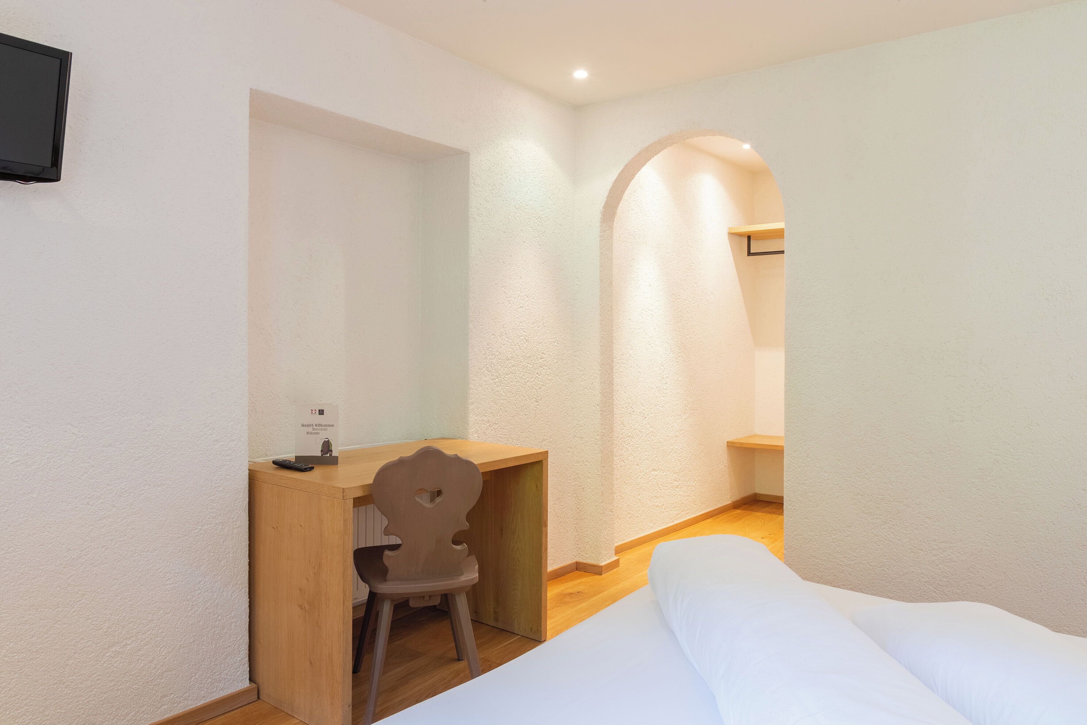 Quarto com uma cama, uma escrivaninha de madeira e uma cadeira.
