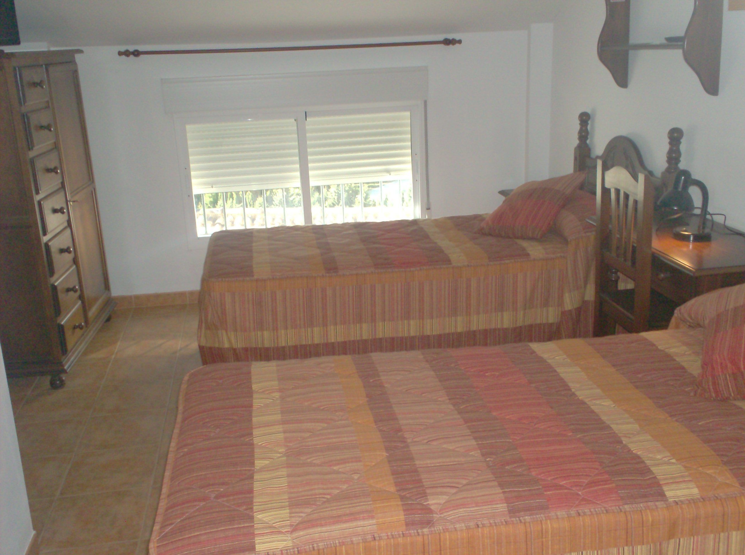 Quarto com duas camas, uma cômoda e uma janela com persianas.