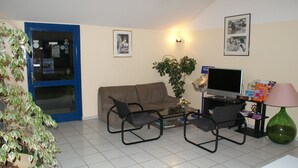 Sala de estar com sofá, duas poltronas, mesa de centro, televisão, luminária e um vaso de planta.