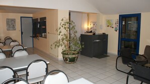 Uma área de refeições com mesas e cadeiras, um vaso de planta, um balcão de recepção e uma porta com moldura azul.