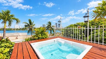 Um deck de madeira com hidromassagem, palmeiras e vista para o horizonte urbano.