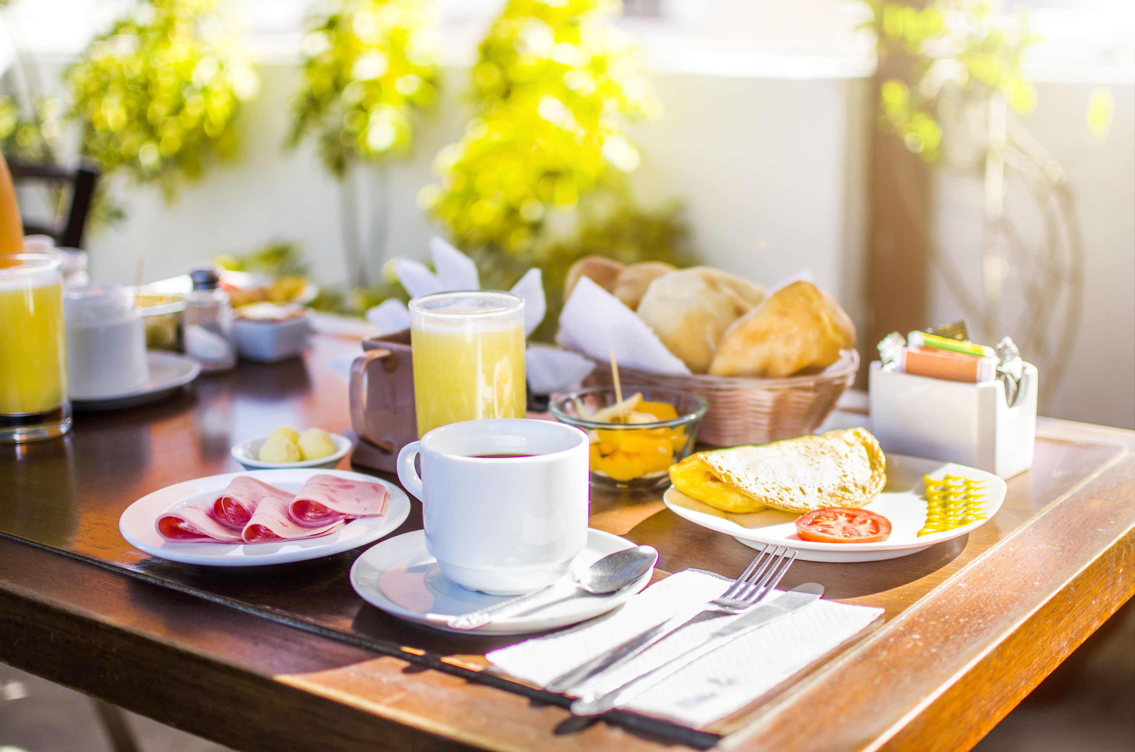 Uma mesa de café da manhã com pratos de comida, uma xícara de café e uma cesta de pão.