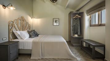 Quarto com uma cama grande, cabeceira de madeira, mesa de cabeceira, um banquinho, luminária pendente, quadro emoldurado e janela com cortinas.