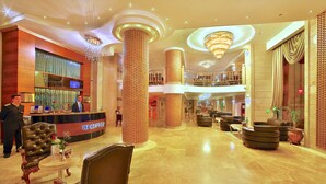 Um lobby amplo com balcão de recepção, poltronas de couro e teto alto com lustres.