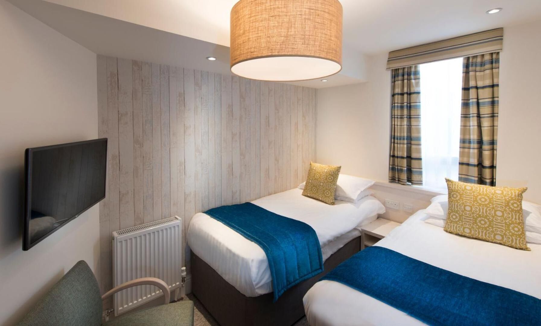 Quarto de hotel com duas camas, televisão de tela plana, radiador e janela com cortinas.