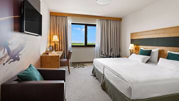 Quarto de hotel com cama, escrivaninha com luminária, cadeira e televisão.