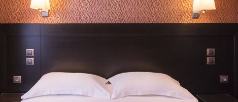 Quarto de hotel com uma cama grande, duas luminárias fixadas na parede e uma parede com padrão.