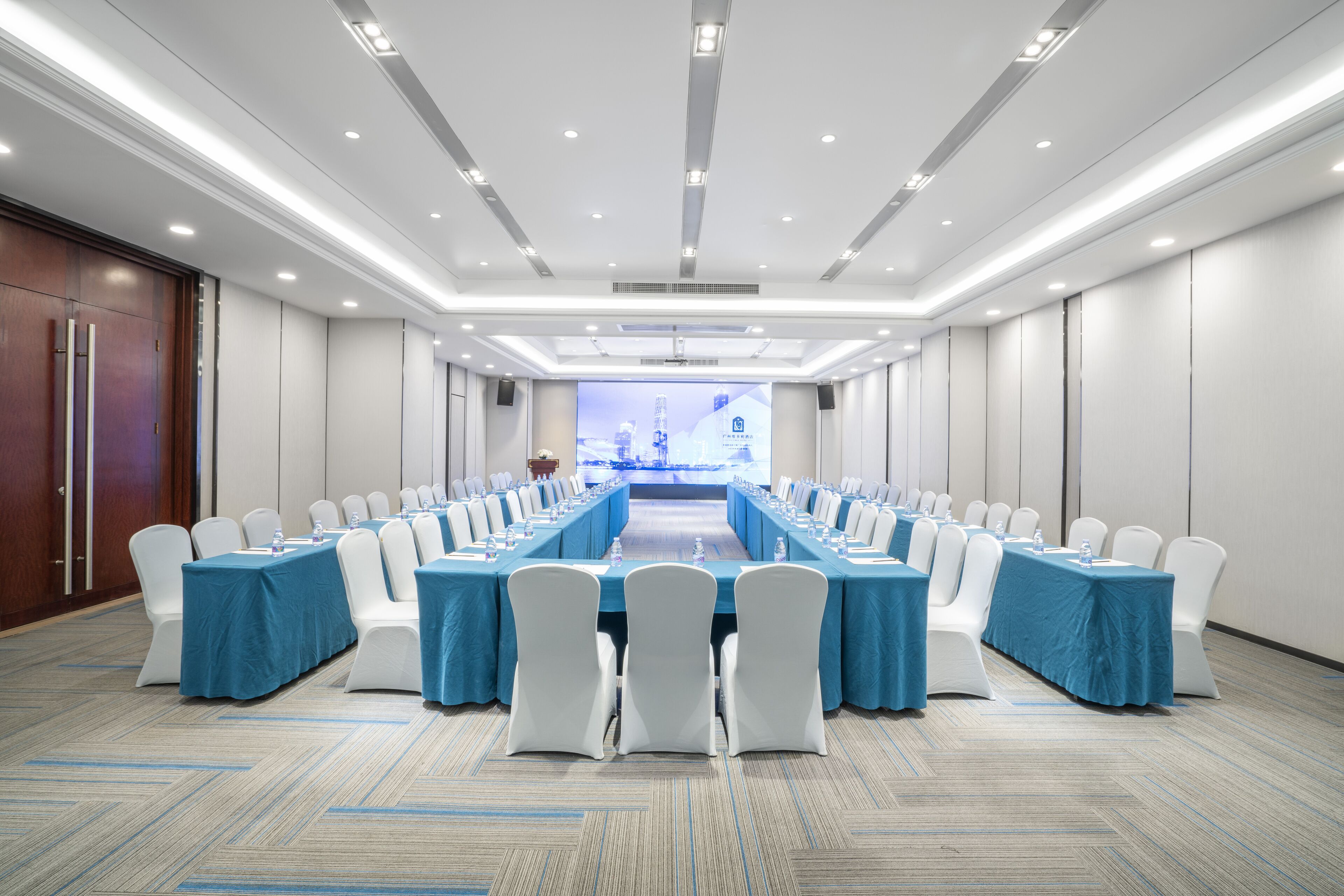 Uma sala de conferências com uma mesa comprida, cadeiras brancas e toalhas de mesa azuis.