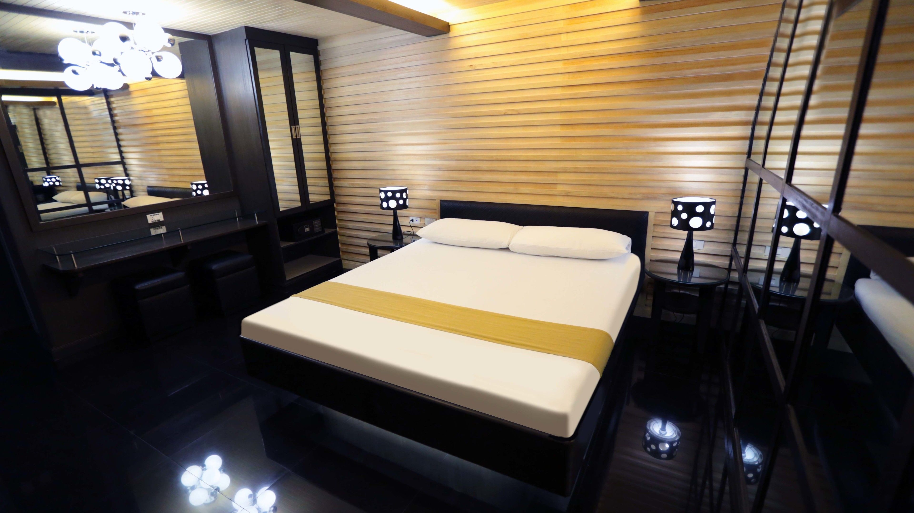 Quarto de hotel moderno com uma cama grande, uma toucador com espelho e duas luminárias de cabeceira.