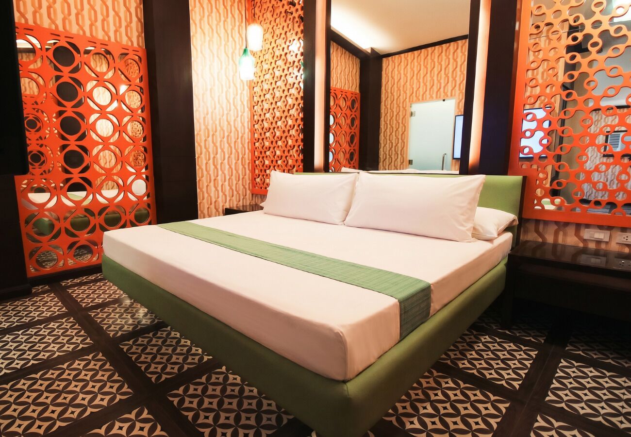 Uma cama com cabeceira verde, roupa de cama branca e piso estampado.