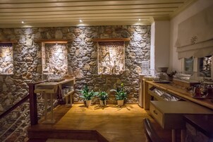 Cozinha com paredes de pedra, bancadas de madeira, plantas em vasos e um ambiente rústico.