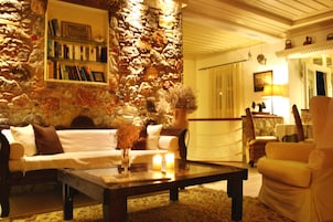 Uma sala de estar acolhedora com parede de pedra, estante de livros, mesa de centro com velas e um sofá confortável.