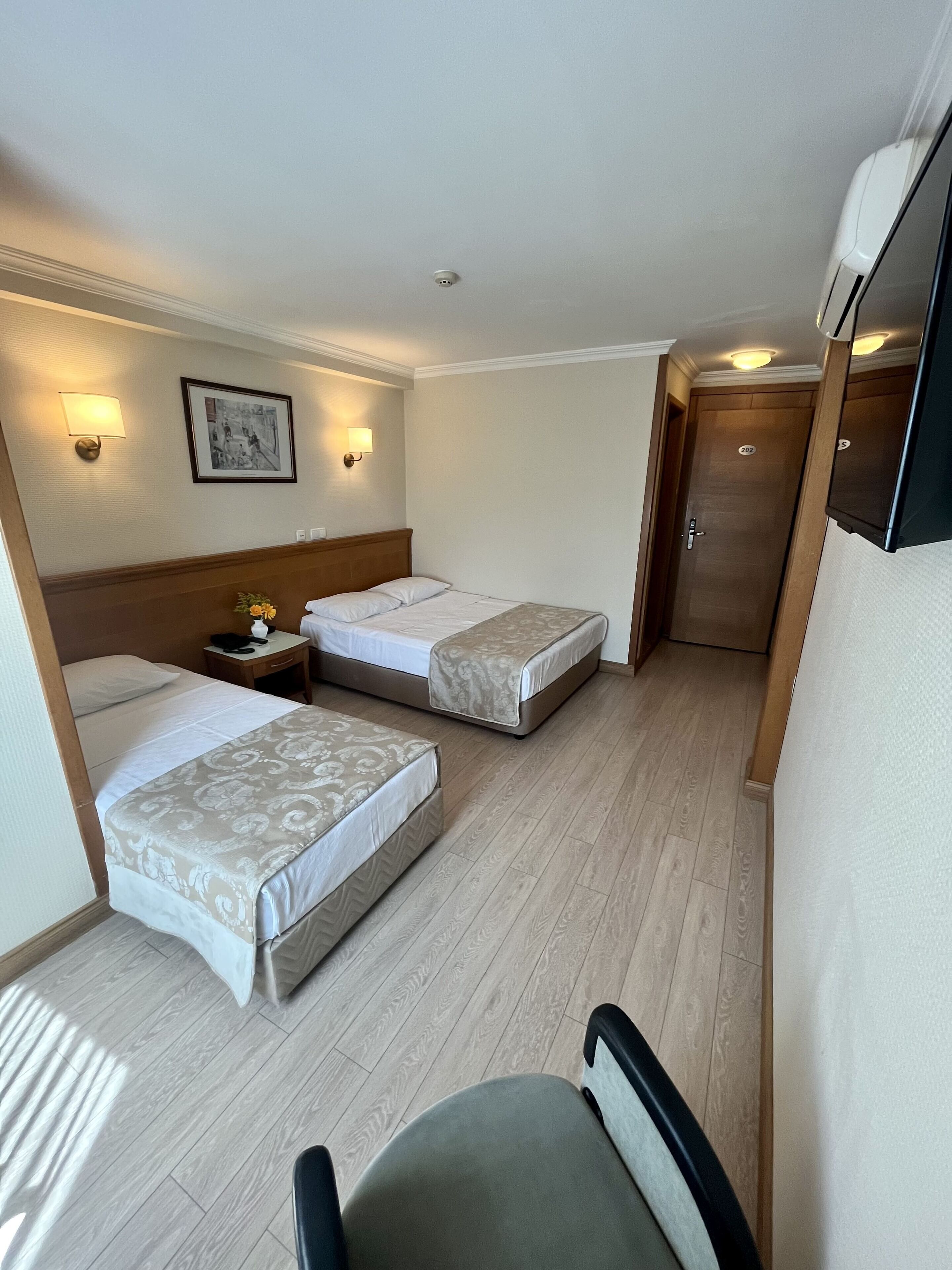 Quarto de hotel com duas camas, uma escrivaninha, uma cadeira e um guarda-roupa.