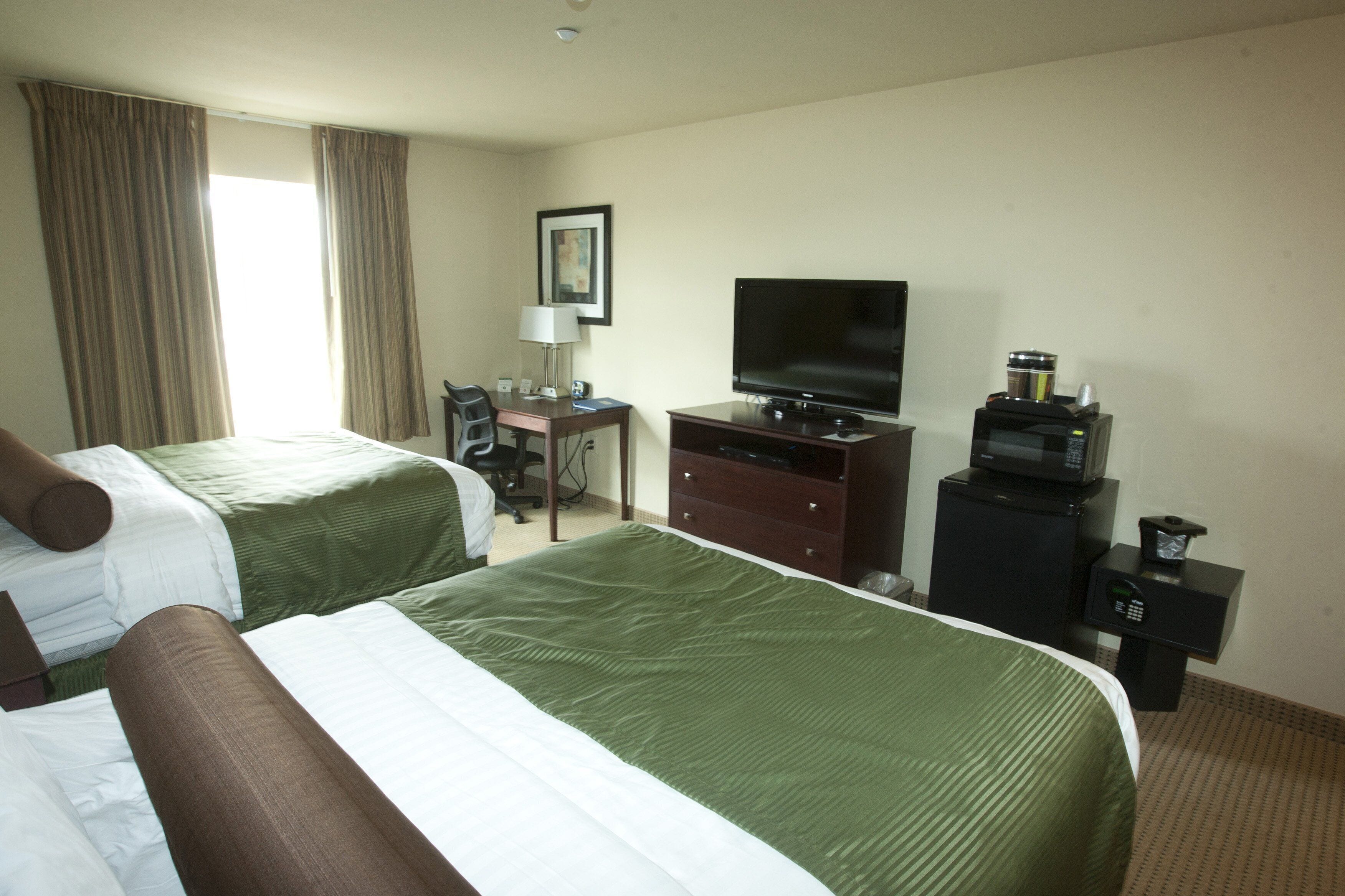 Quarto de hotel com duas camas, uma escrivaninha, televisão e máquina de café.