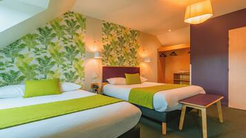 Quarto de hotel com duas camas, uma mesinha e um banheiro visível ao fundo.