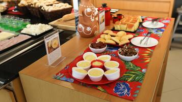 Uma mesa de buffet com diversos alimentos, incluindo doces, patês e uma figura decorativa de cerâmica.