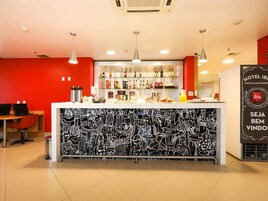 Uma área de recepção de hotel com bar, balcão e uma parede com mural em preto e branco.
