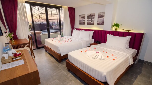 Quarto de hotel com duas camas, uma mesa, uma cadeira e uma janela com vista.
