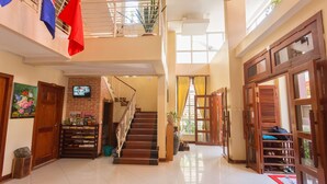 Um hall amplo com escada, televisão fixada em parede de tijolos e um apoio para sapatos.
