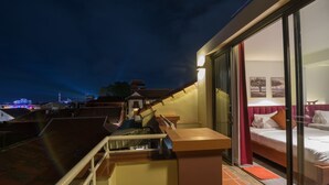 Quarto de hotel com varanda, cama com almofadas e vista noturna da cidade.