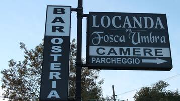 Uma placa de direção com 'BAR OSTERIA' e 'LOCANDA FoscA Umbra CAMERE PARCHEGGIO' apontando para a direita.