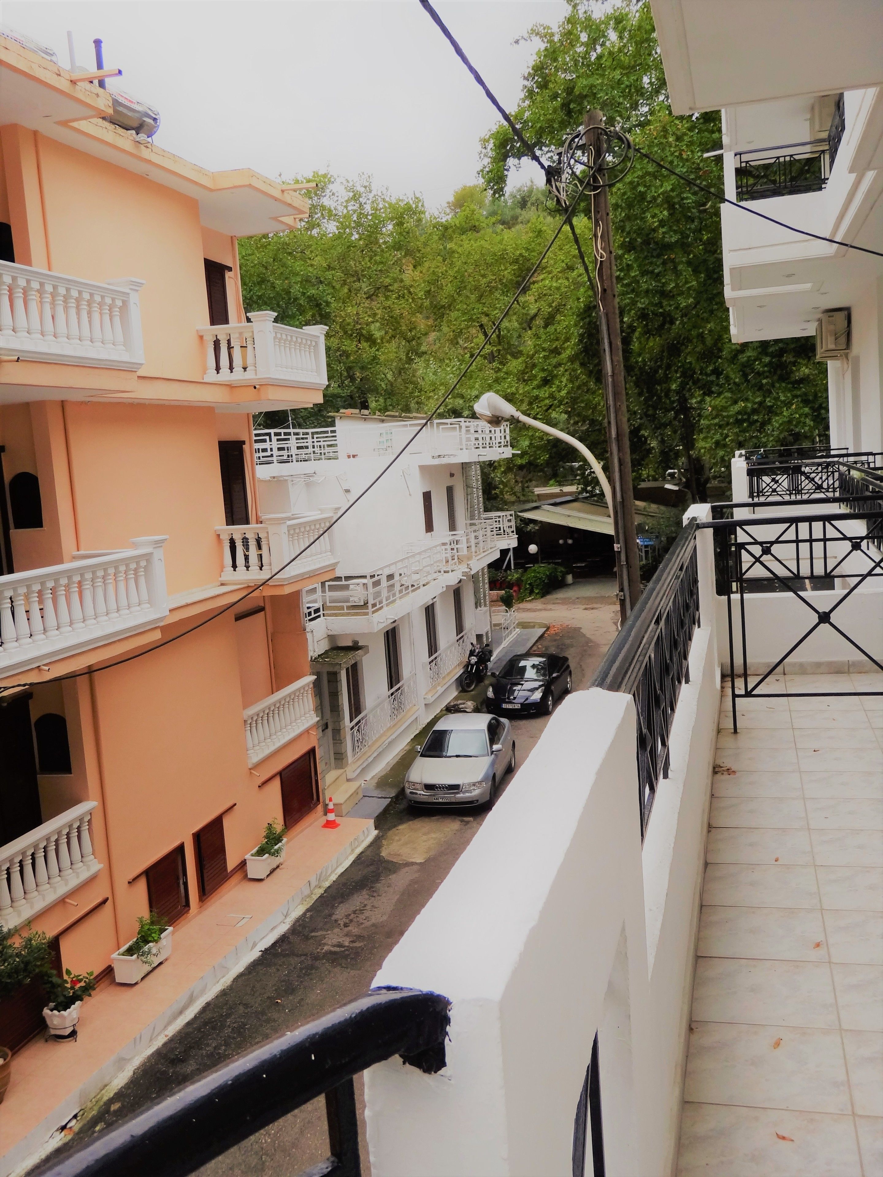Um edifício residencial com varandas, uma rua estreita, carros estacionados e uma linha de energia visível.