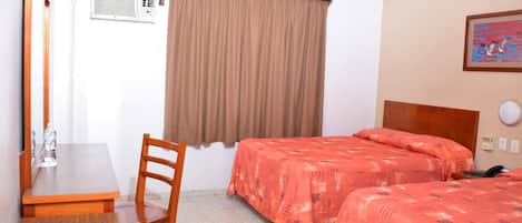 Quarto de hotel com duas camas, uma escrivaninha, uma cadeira, uma janela com cortinas e um quadro na parede.