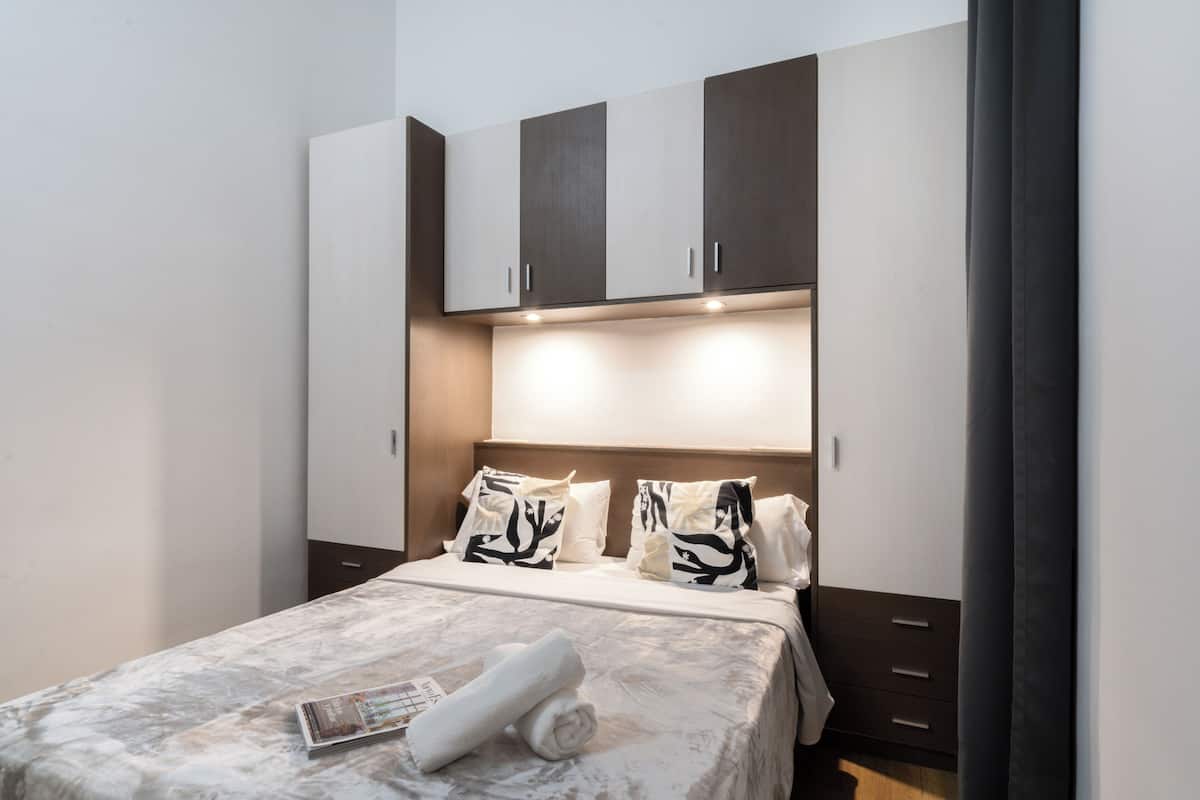Quarto com cama, mesa de cabeceira, uma revista e uma toalha enrolada.
