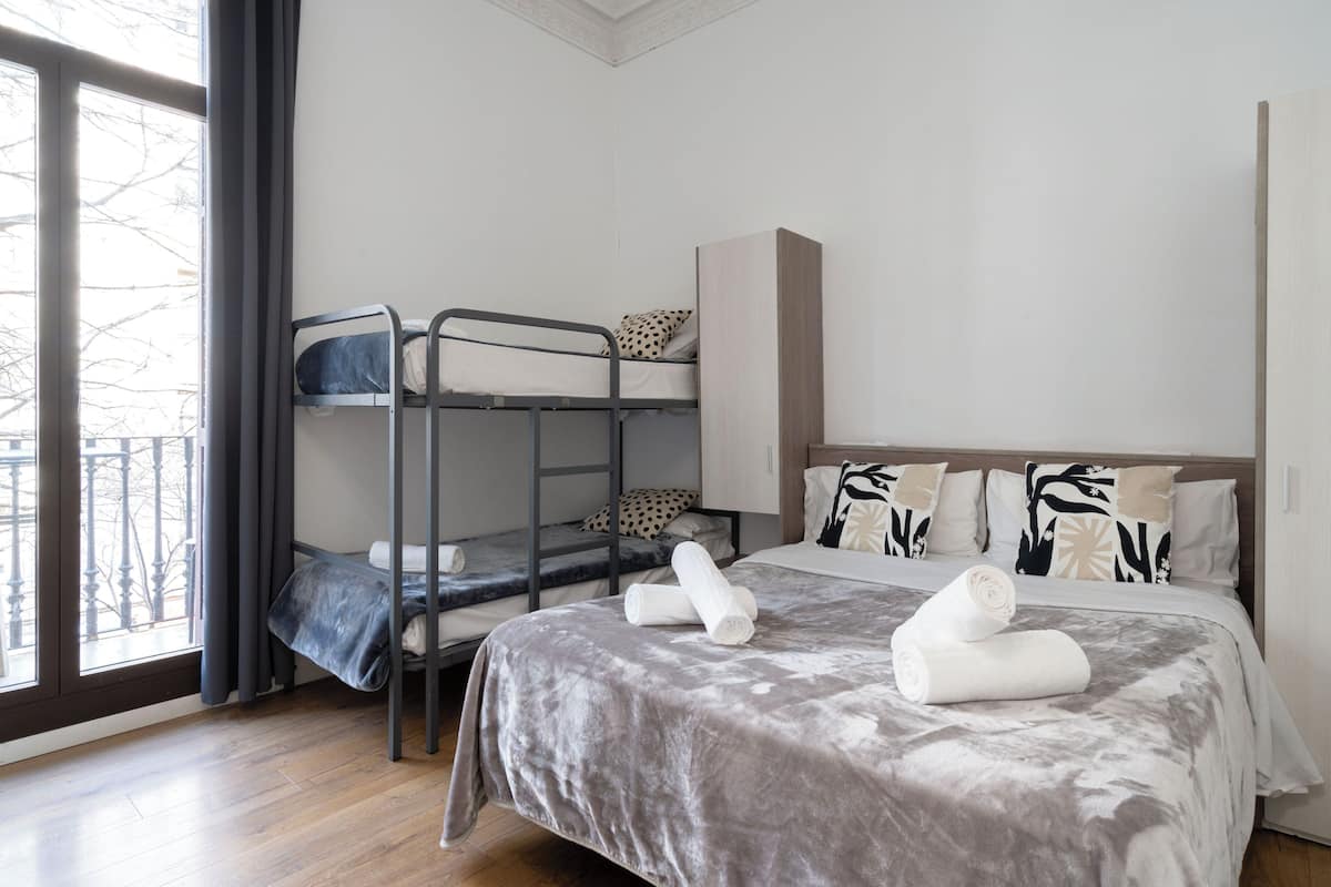 Quarto com cama de solteiro, cama com toalhas enroladas e vista para uma varanda.