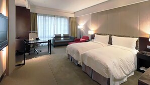 Quarto de hotel com uma cama grande, uma escrivaninha, uma cadeira, uma televisão e uma janela com cortinas.
