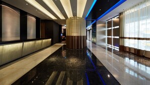 Um hall de hotel moderno com piso de mármore polido, uma coluna central e um balcão de recepção extenso.
