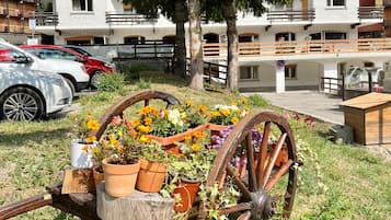 Um edifício moderno com varandas, área de estacionamento e um carrinho com plantas em vasos.