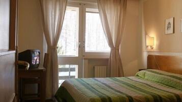 Quarto de hotel com cama, escrivaninha com luminária e janela com cortinas.