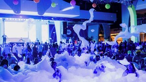 Um evento interno lotado, com pessoas aproveitando uma área de atividades com espuma.