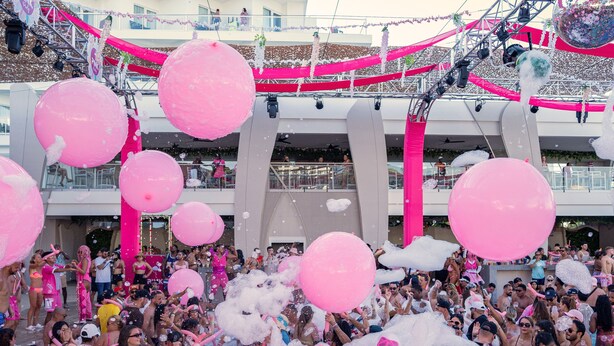 Um evento interno lotado, com decorações cor-de-rosa e balões grandes.