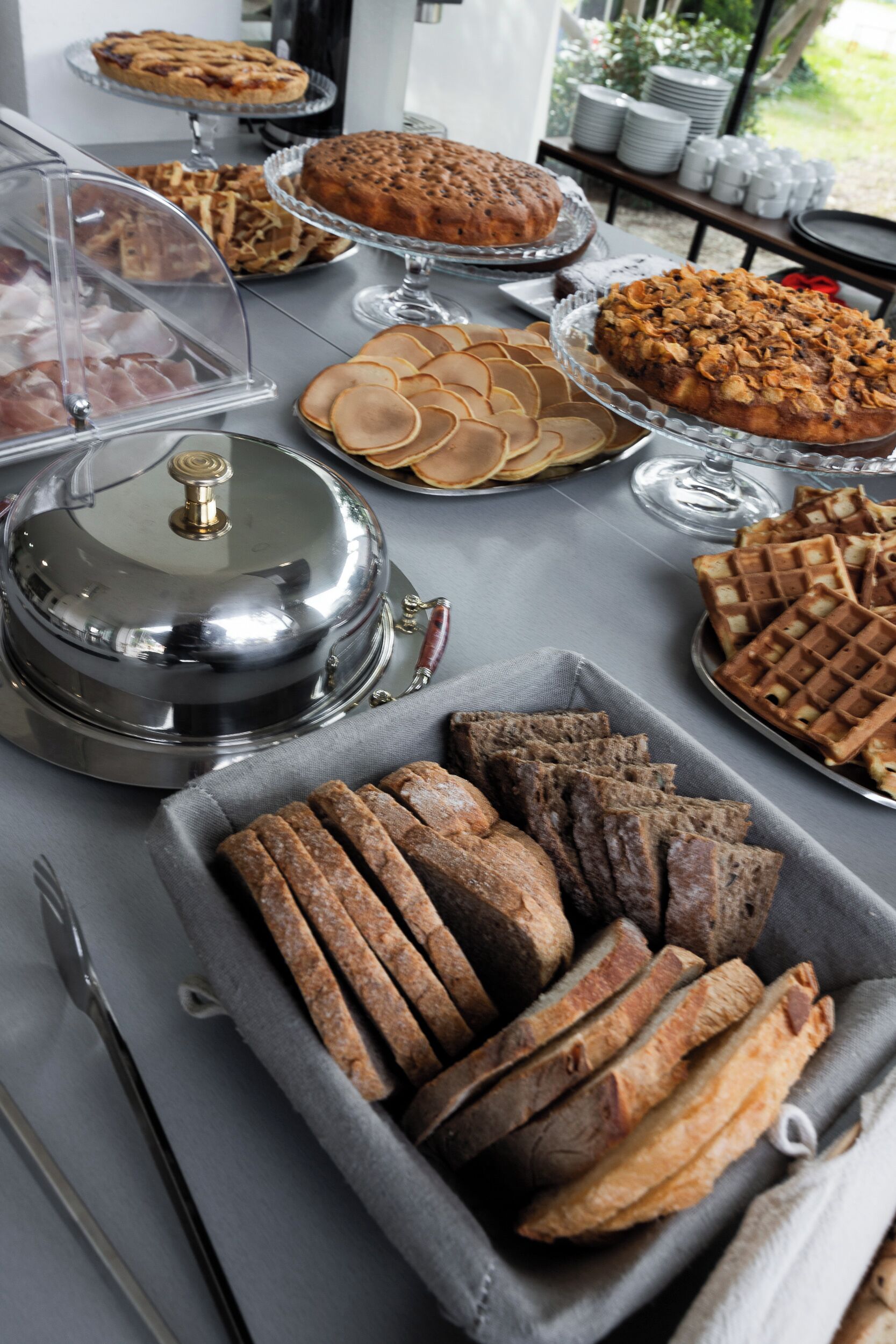 Uma mesa de buffet com diversos produtos de panificação, incluindo pão, pastelaria e um recipiente tampado.