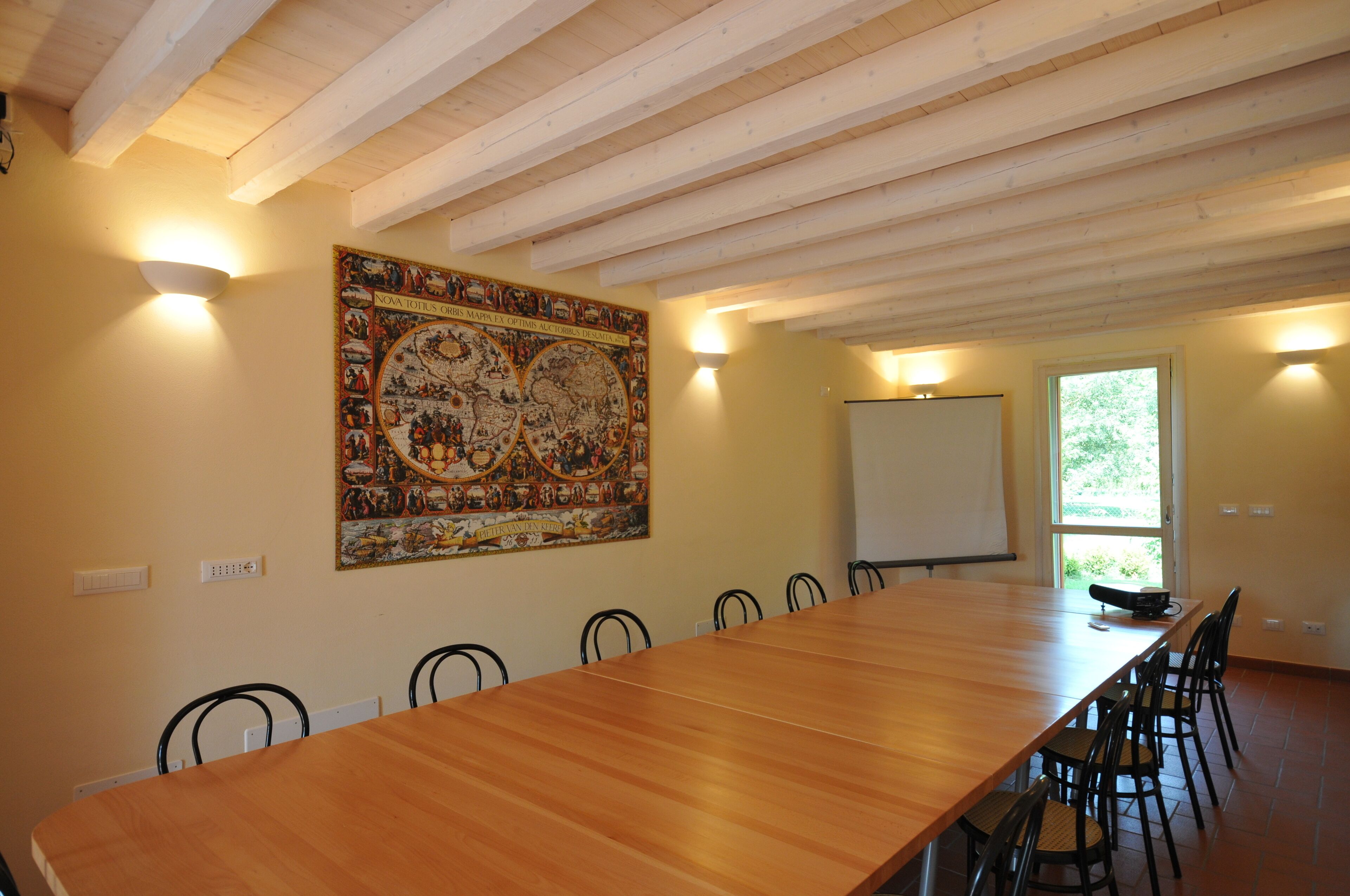 Uma sala de conferências com uma longa mesa de madeira, cadeiras pretas, um grande mapa histórico na parede e uma lousa.