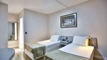 Quarto de hotel com duas camas, uma mesa de escritório, uma cadeira, mesa de cabeceira, abajur e um quadro na parede.