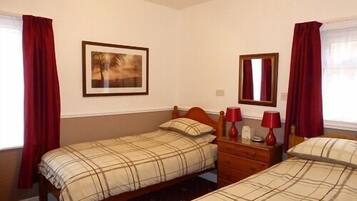 Quarto com duas camas, cabeceira de madeira, mesa de cabeceira com luminárias, um quadro na parede e cortinas vermelhas.