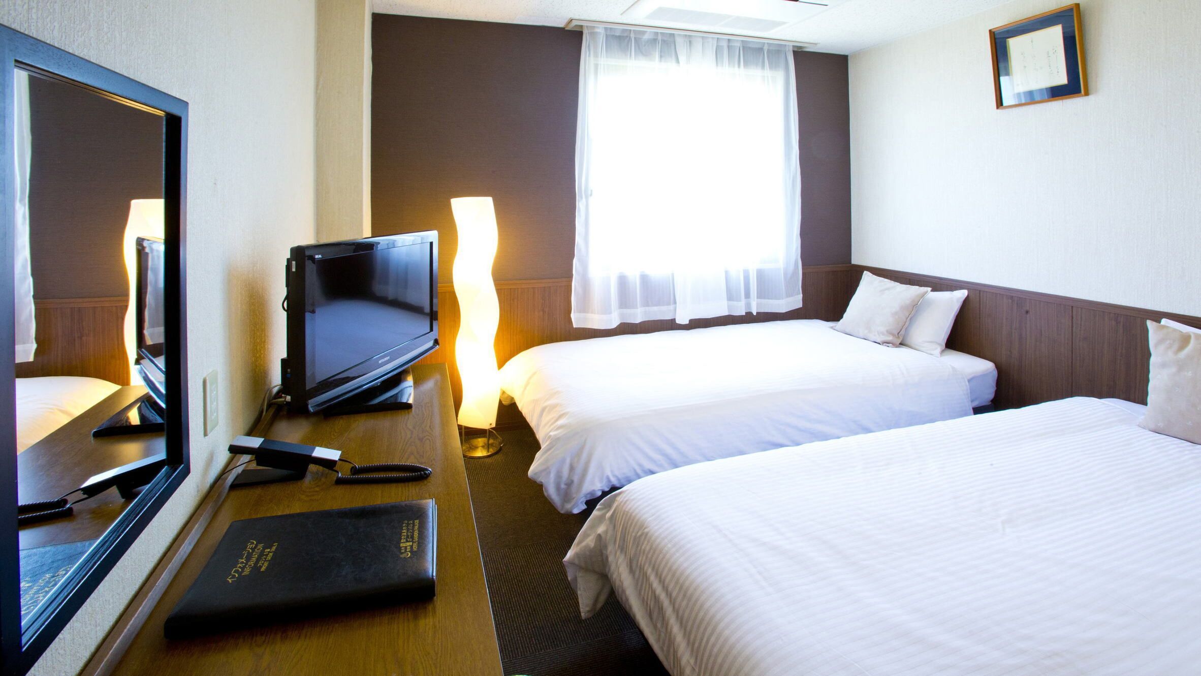 Quarto de hotel com cama, escrivaninha, televisão, telefone e luminária.