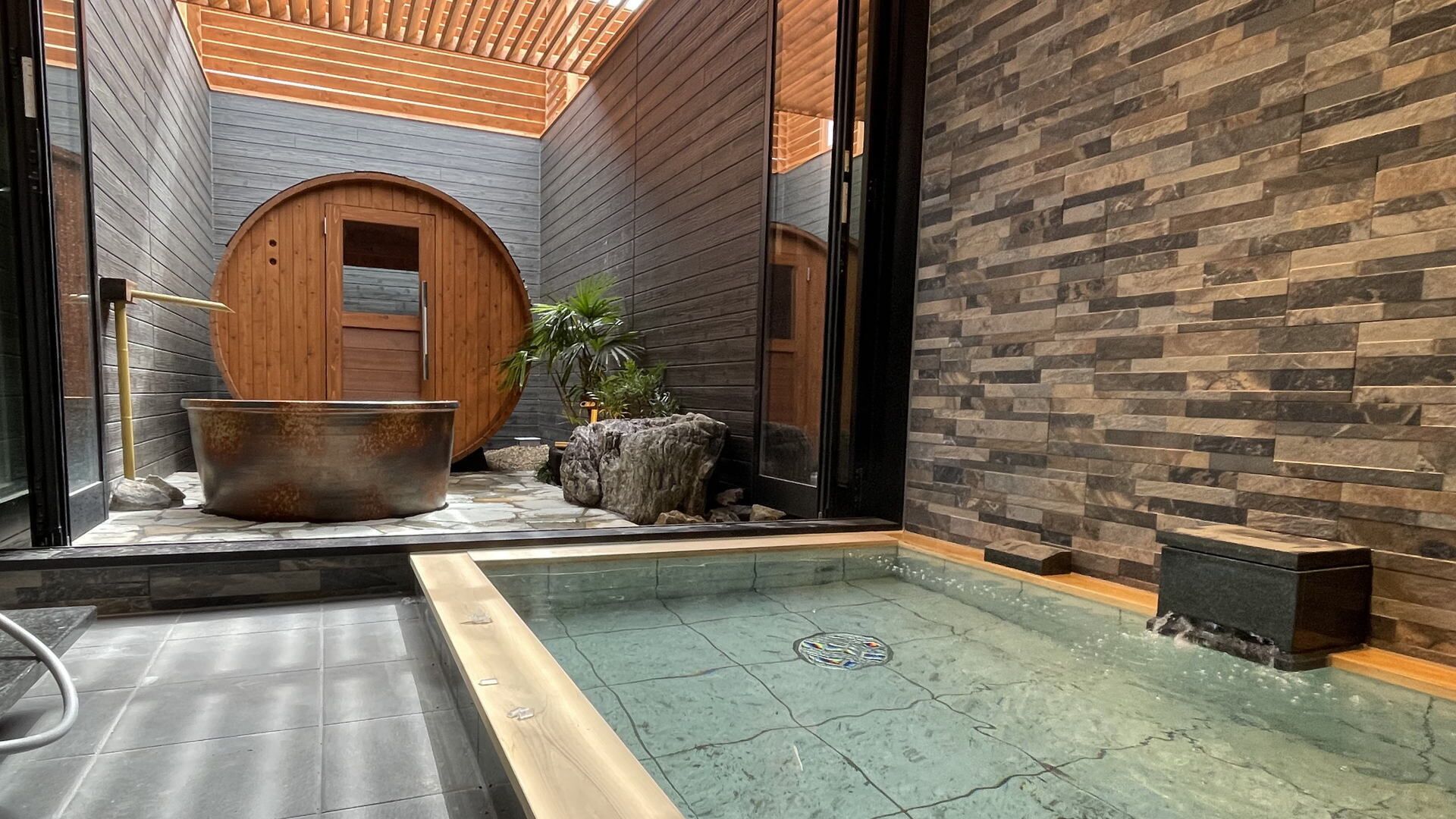 Uma área de spa com piso de pedra, banheira de hidromassagem de madeira e parede de pedra.
