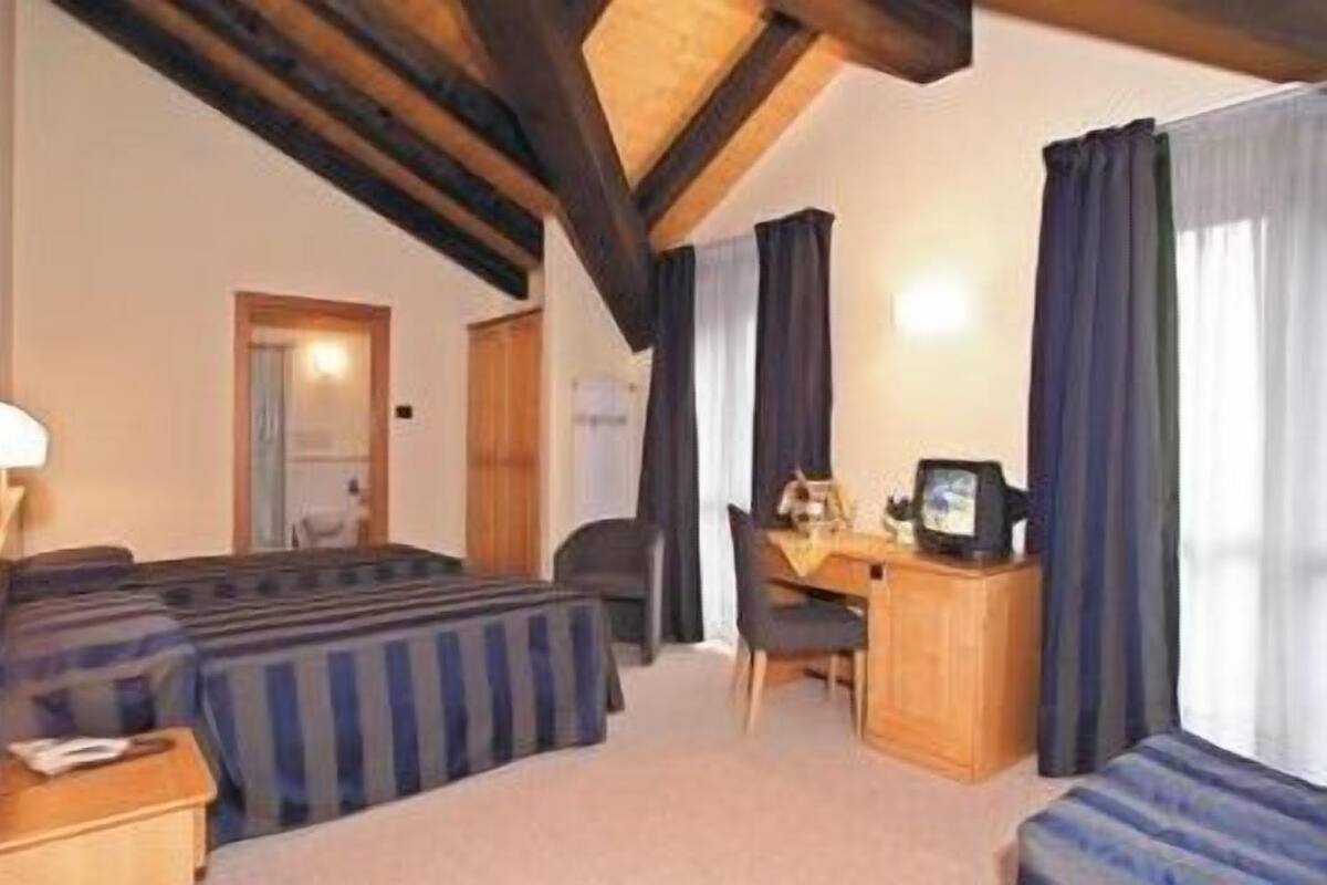 Quarto de hotel com cama, escrivaninha, cadeira e televisão.