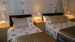 Quarto de hotel com duas camas, cada uma acompanhada de mesa de cabeceira, abajur e pequena mesa.