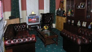 Uma sala de estar com um sofá de couro, uma mesa de centro de vidro e uma televisão.