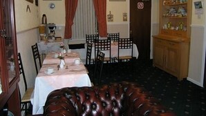 Uma sala de jantar com uma mesa posta para quatro pessoas, um sofá de couro e uma área de cozinha com armários e uma geladeira.