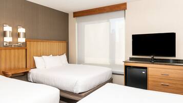 Quarto de hotel com duas camas, televisão, frigorífico e janela com persianas.